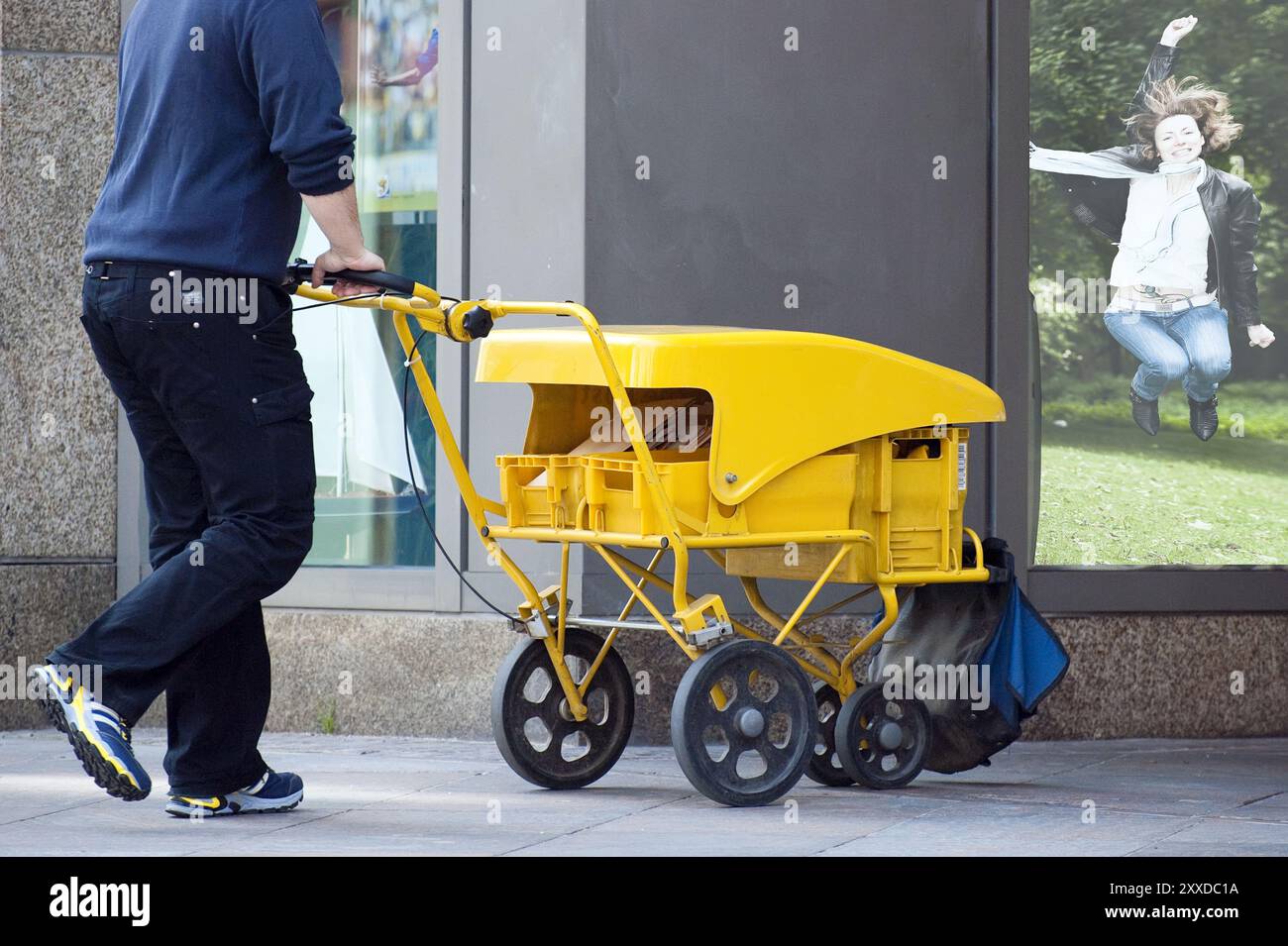 Postman with trolley in front of shop window with young woman jumping ...