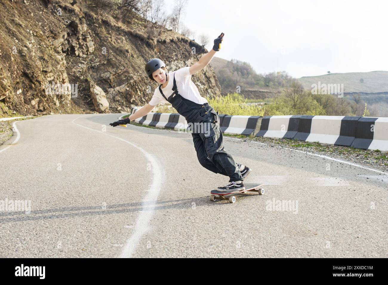A young rider on a longboard in a helmet and gloves overall performs a ...
