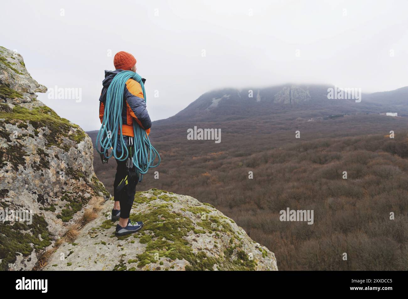 A professional mountaineer in a red down jacket with a bay of blue rope ...