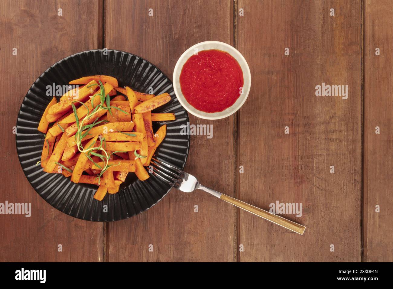Sweet potato fries with rosemary and ketchup, shot from above on a dark ...