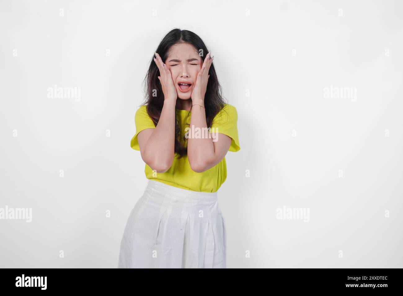 Stressed Asian woman in a yellow shirt and white skirt holding her chin ...