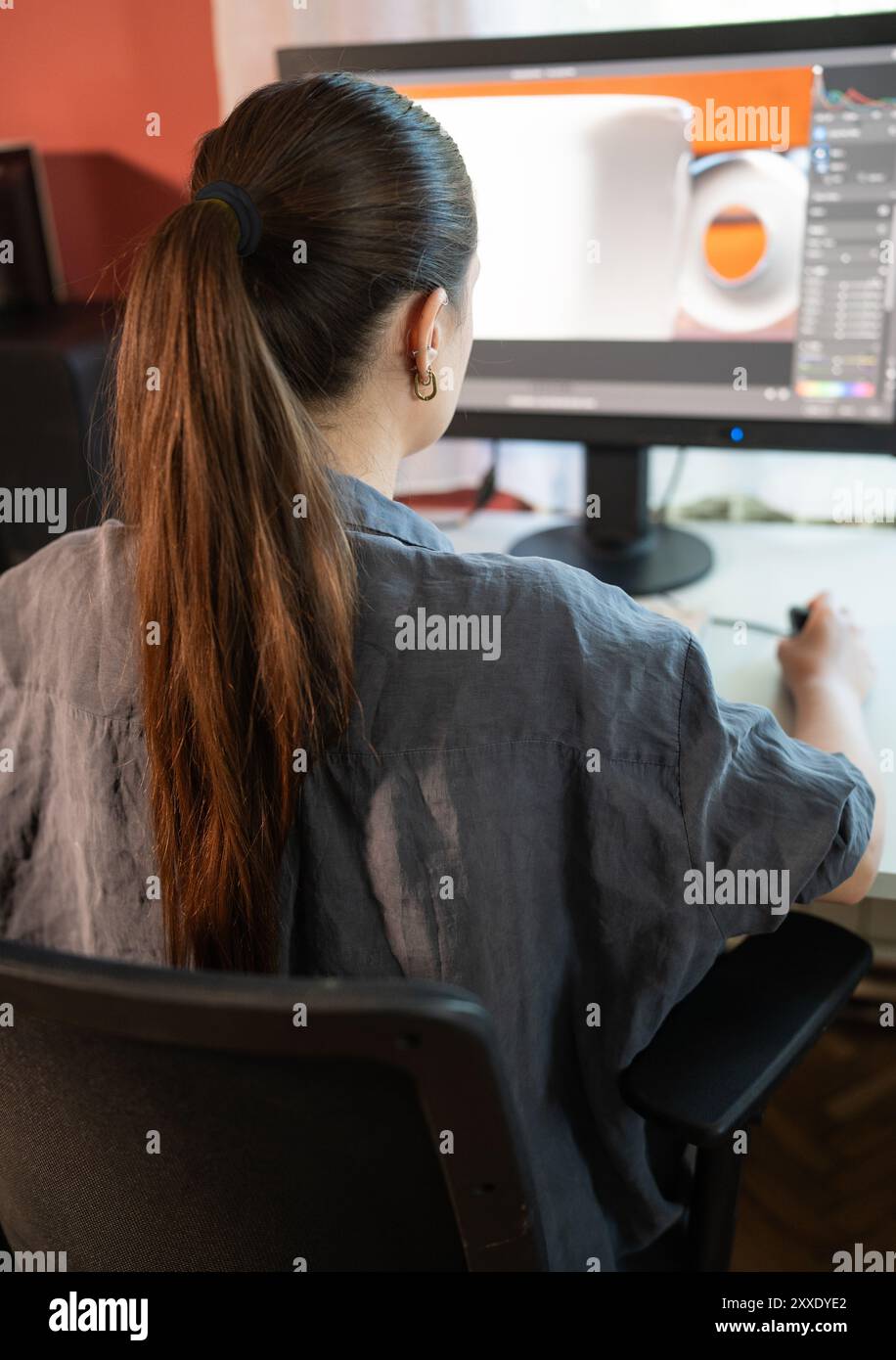 A young woman is sitting at a computer in the office, doing graphic ...