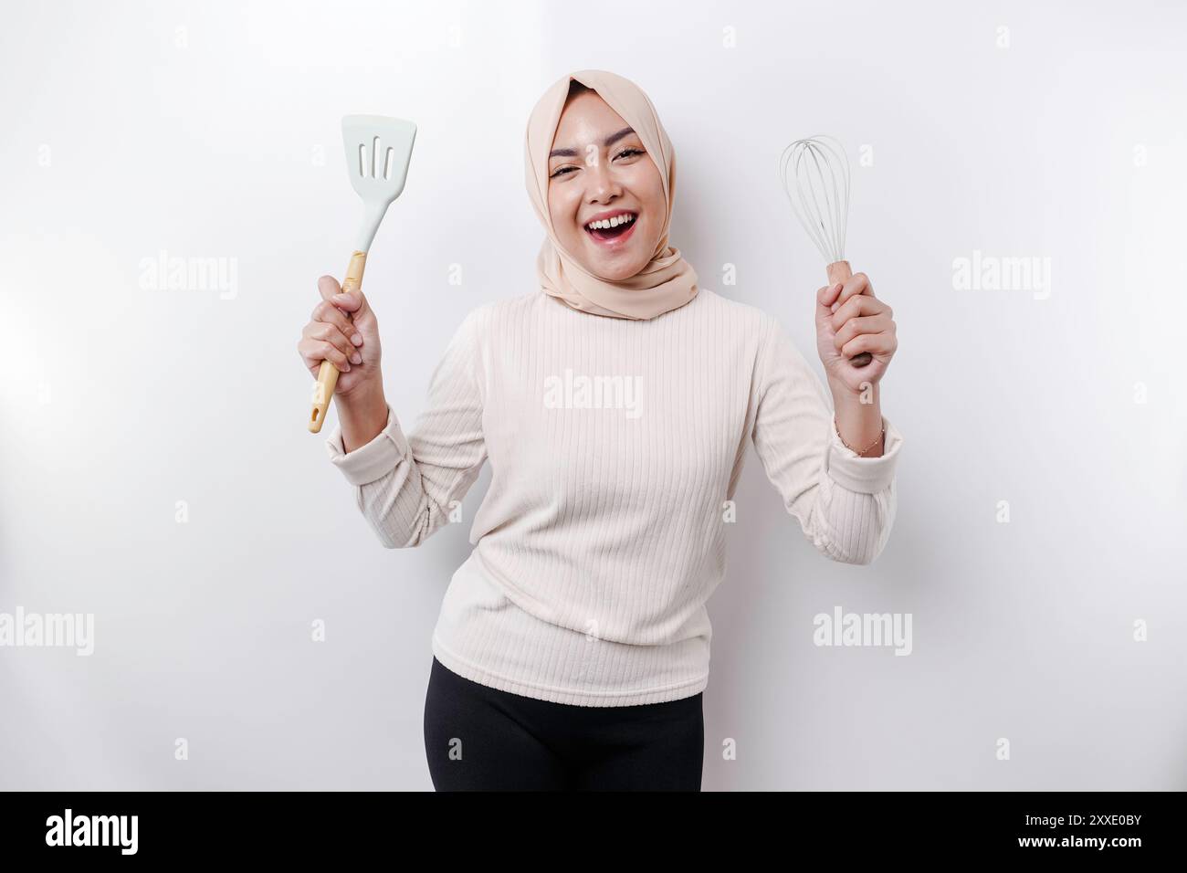 Excited Asian Muslim woman wearing a headscarf, holding cooking ware ...