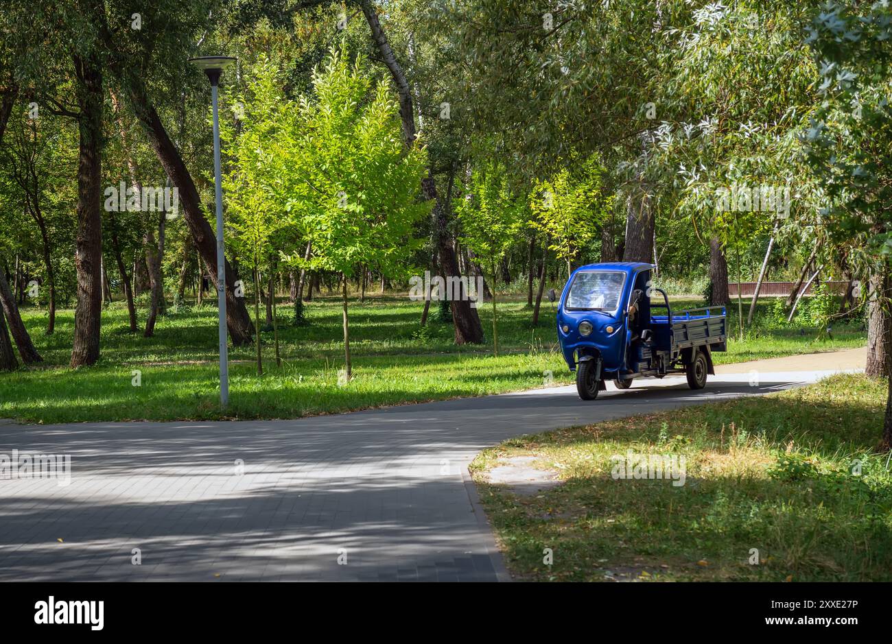 Municipal workers collect garbage in the park with a small blue car ...