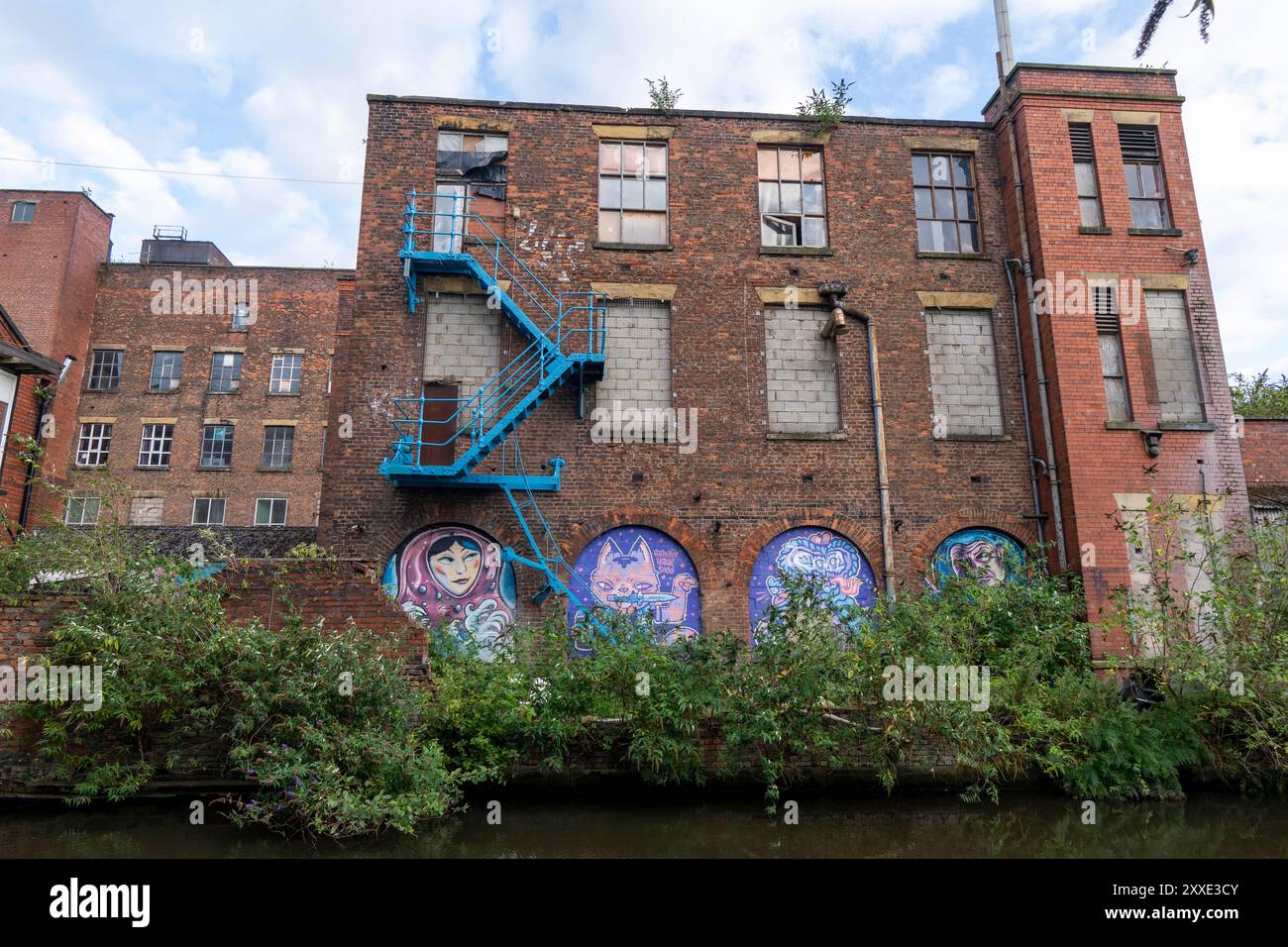 red brick building with many windows and vegetation growing on the roof ...