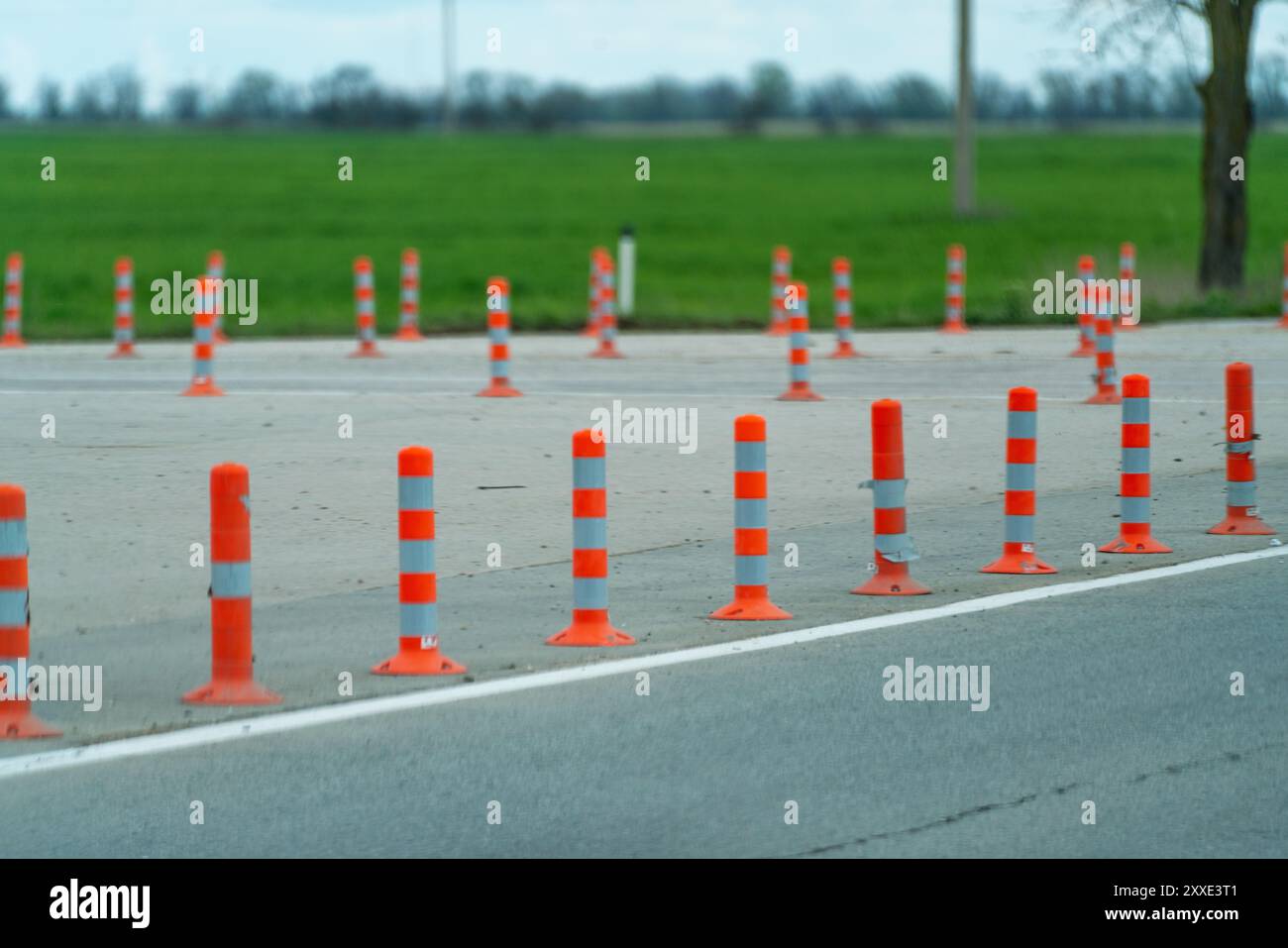 A row of orange and white traffic cones are lined up on a road. The ...