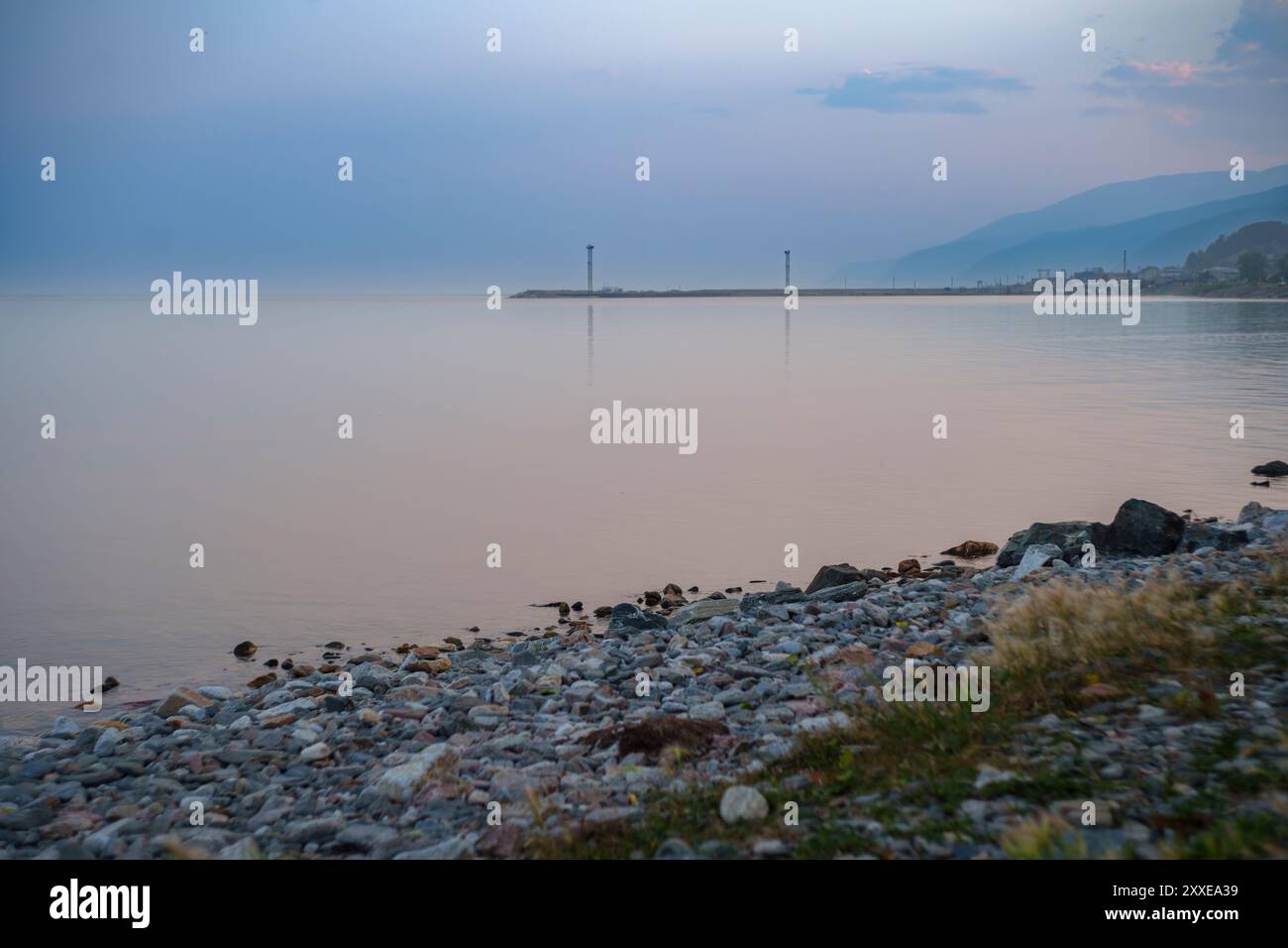 A tranquil scene of a pebble beach with calm, misty waters at dawn ...