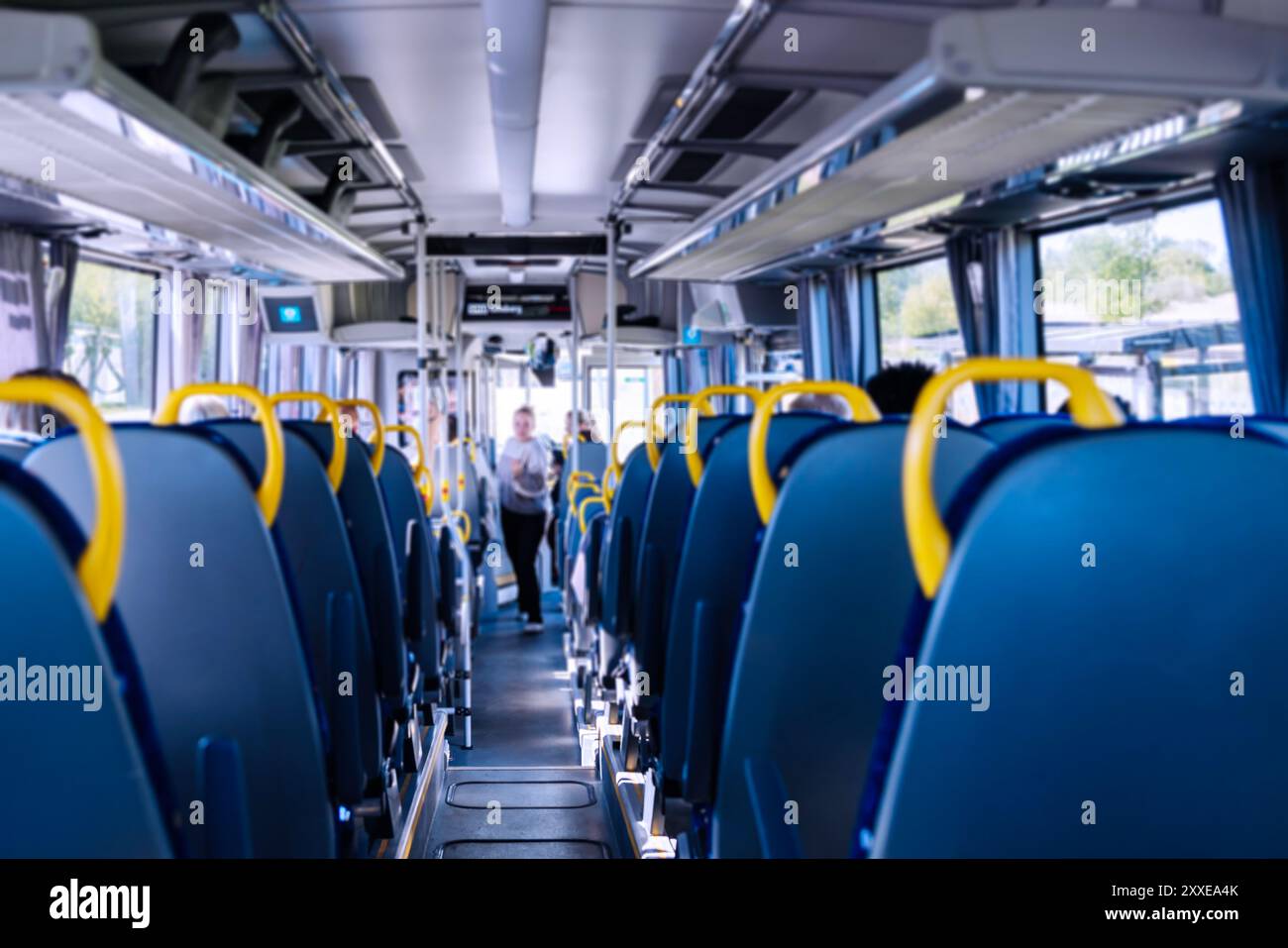 A modern bus interior features empty seats with yellow handles for ...