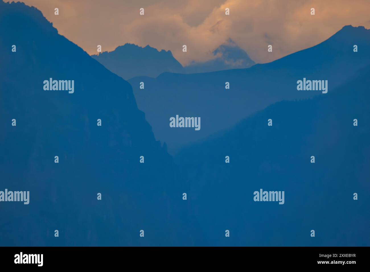 A misty mountain range silhouetted against a cloudy sky at dusk ...
