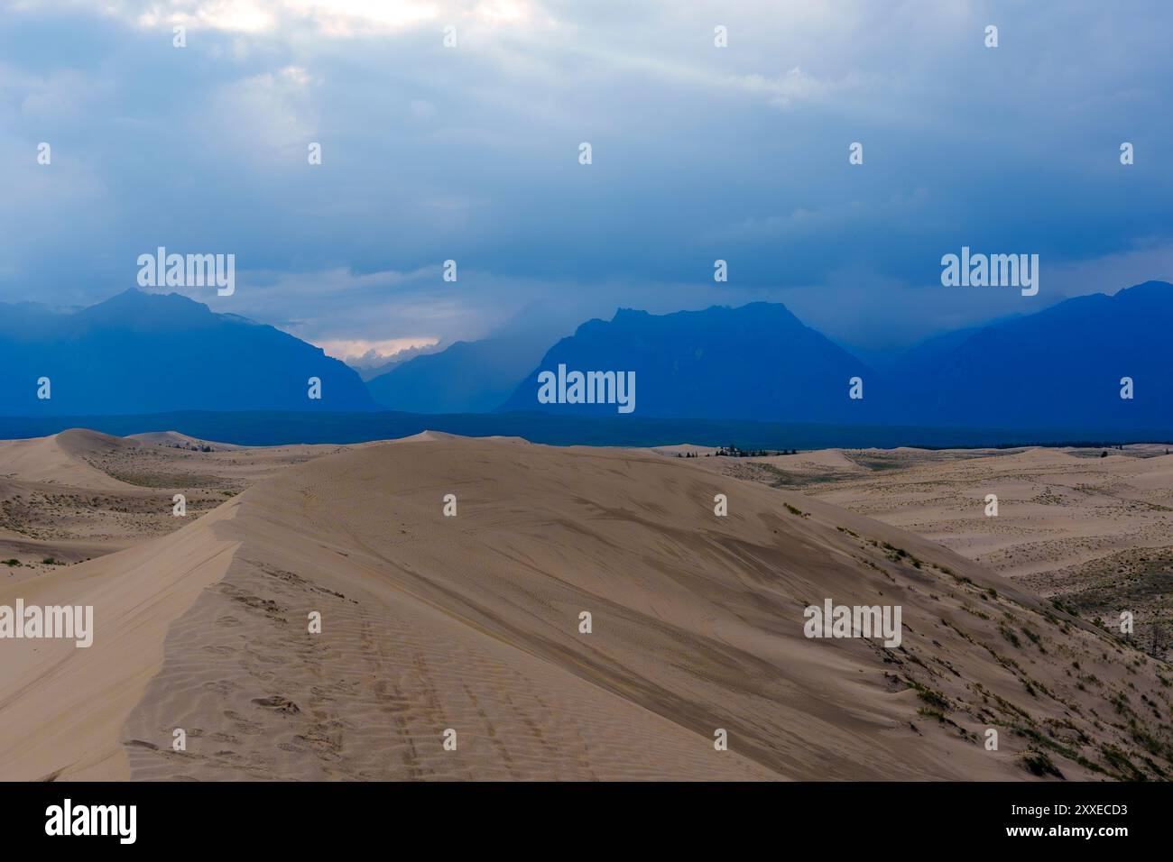 A vast landscape of rolling desert dunes under a dramatic sky, with ...