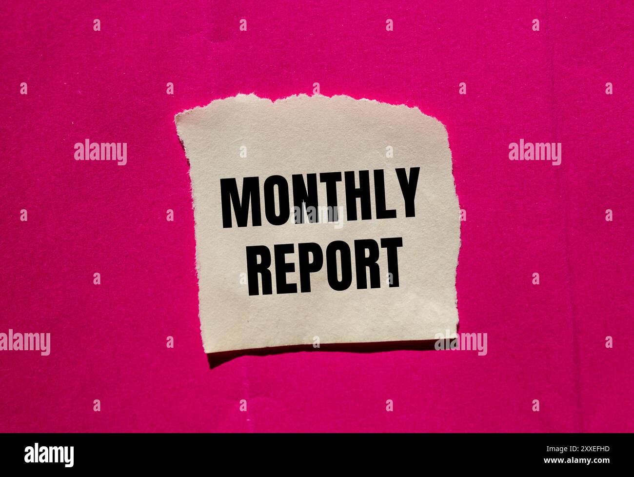 Monthly report message written on ripped torn paper piece on pink ...