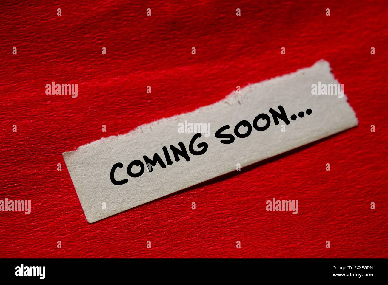 Coming soon message written on torn paper with red background ...