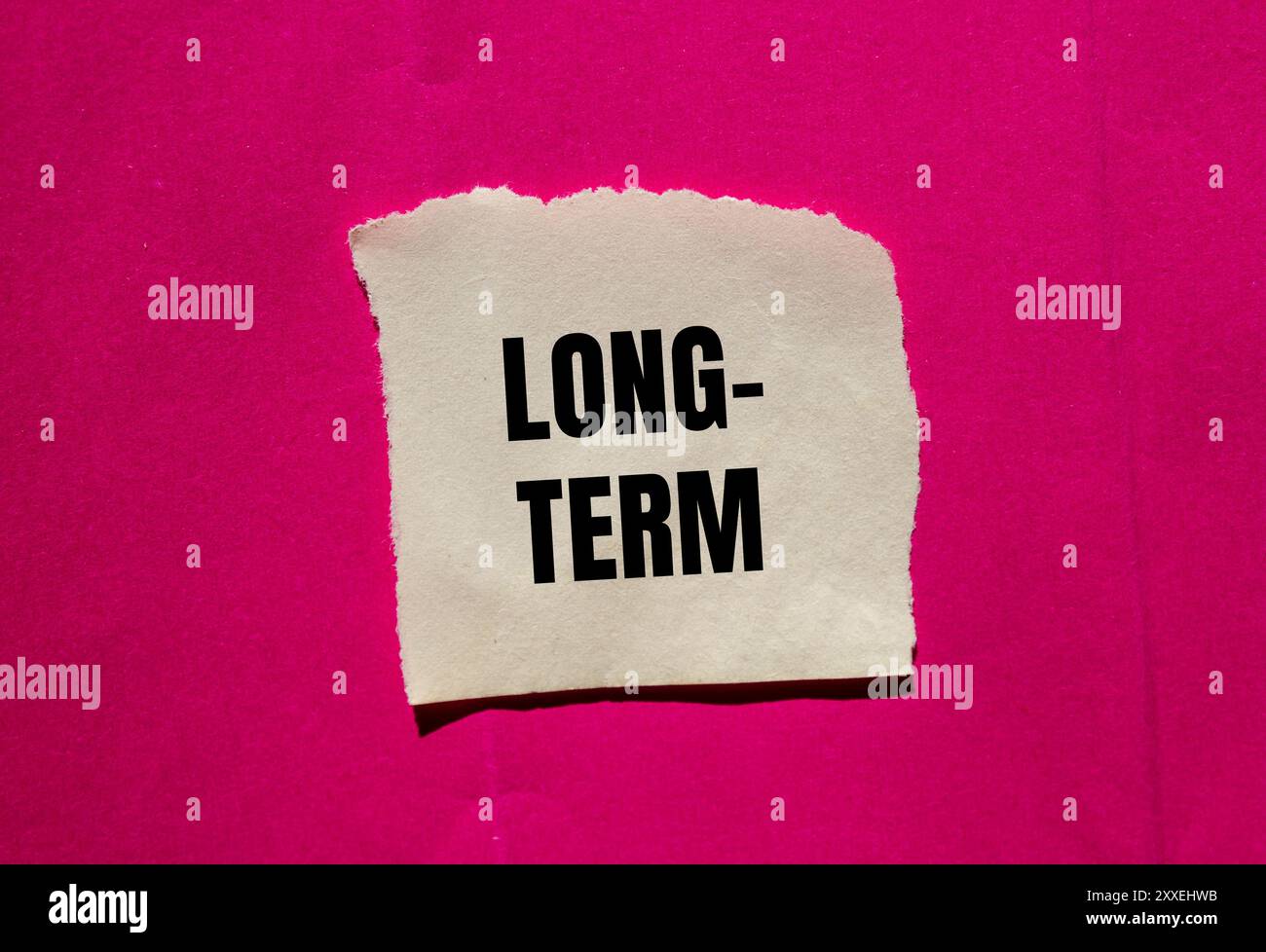 Long term message written on ripped torn paper piece on pink background. Conceptual long term ...