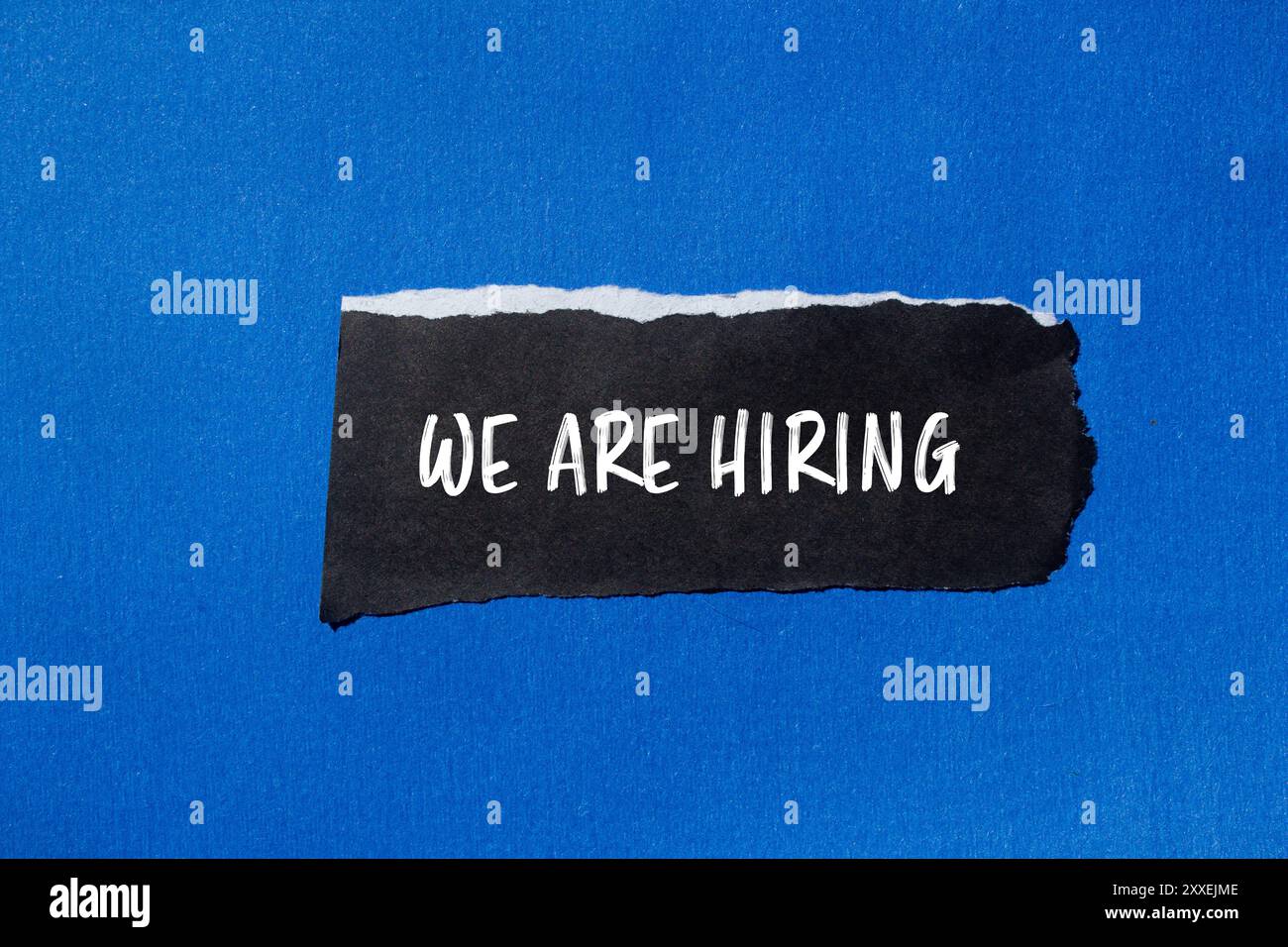 We are hiring message written on ripped torn black paper piece with blue background. Conceptual ...