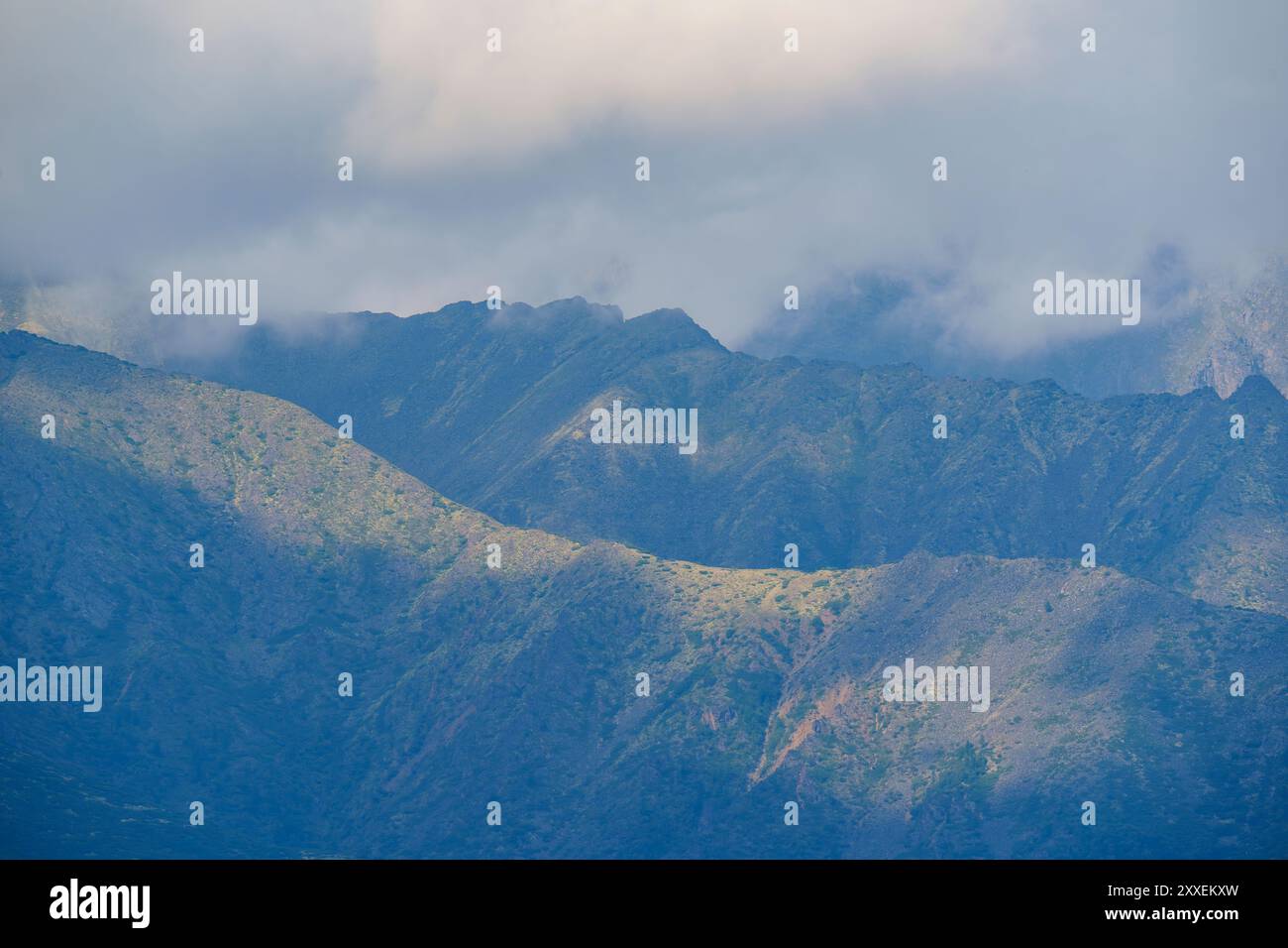 A view of misty mountain peaks partially obscured by clouds, creating a dramatic and atmospheric ...