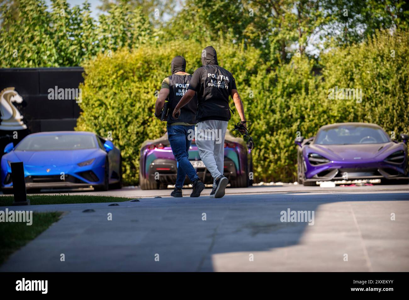 Masked police officers walk backdropped by sports cars at Andrew Tate's ...