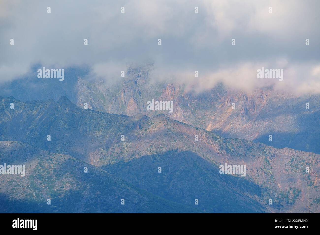 A view of misty mountain peaks partially obscured by clouds, creating a dramatic and atmospheric ...