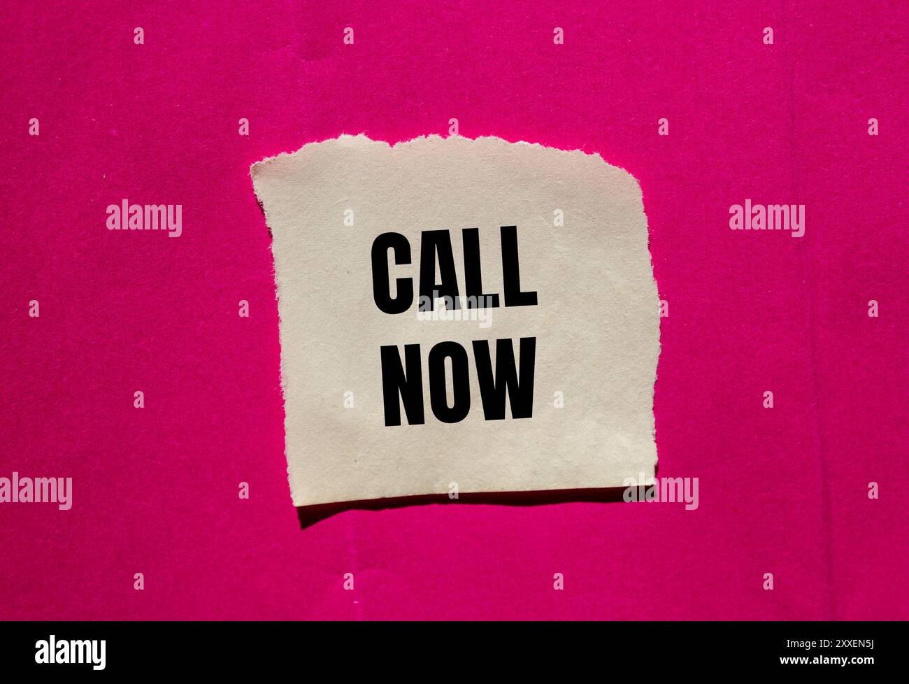 Call now message written on ripped torn paper piece on pink background ...