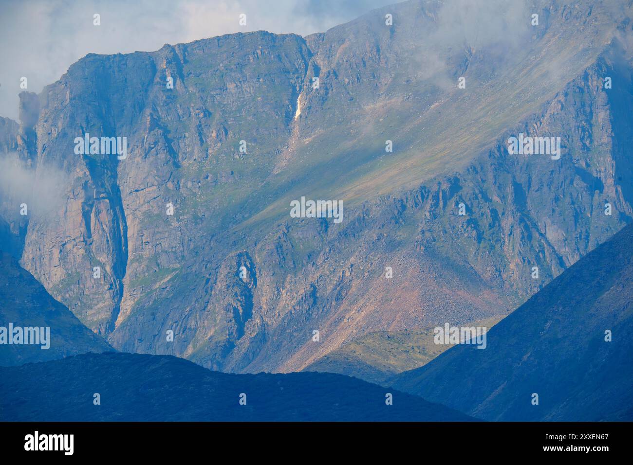 A detailed close-up of rugged mountain cliffs partially shrouded in ...