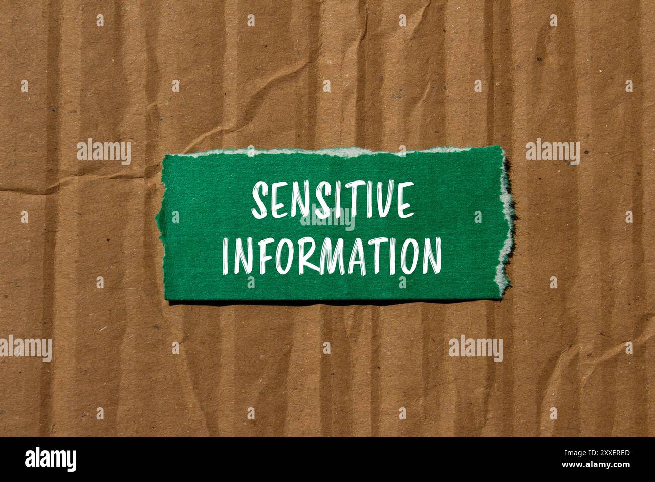 Sensitive information message written on ripped torn green paper piece with cardboard background ...