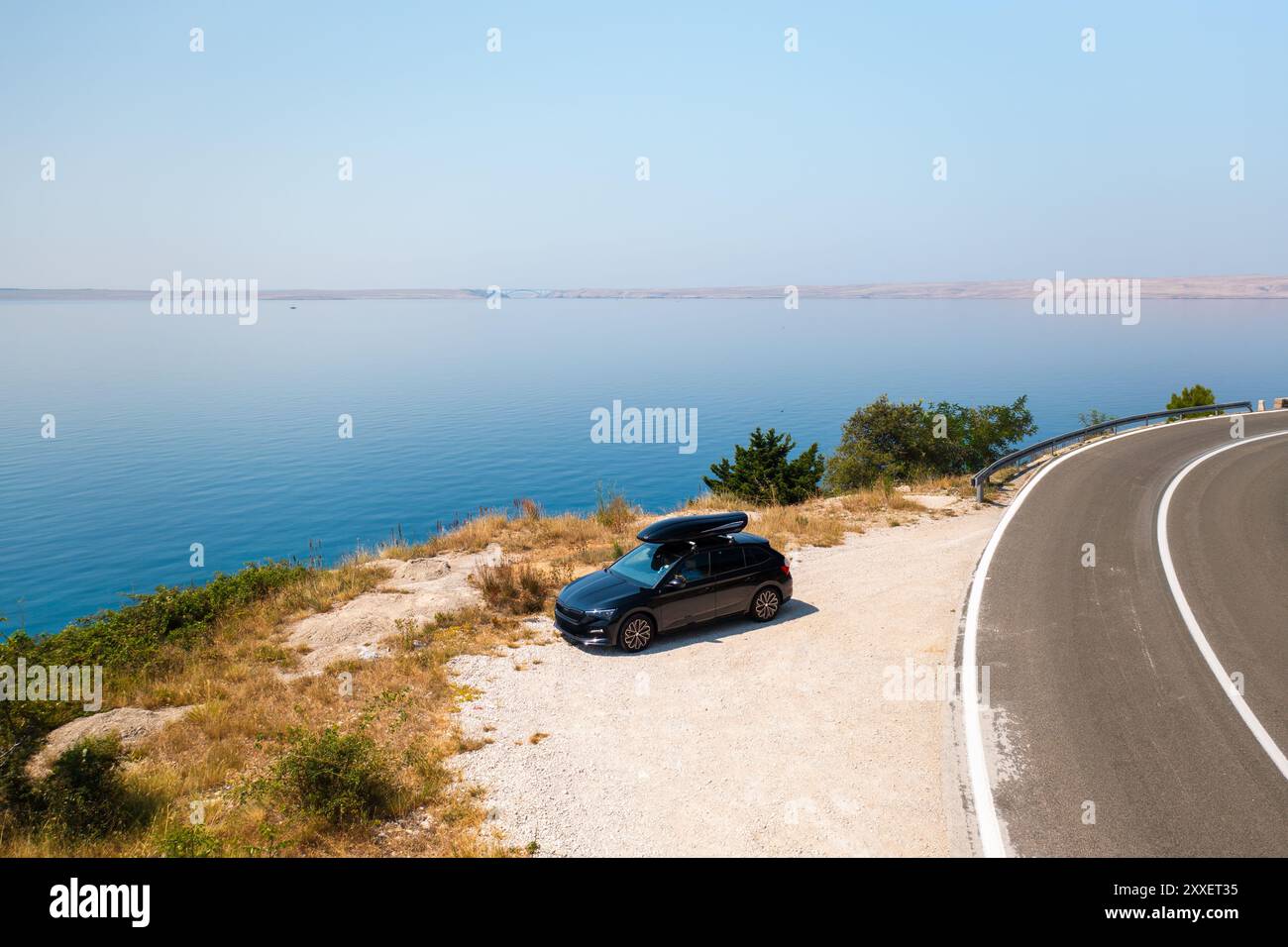 Car with a roof box, parked beside a narrow, winding road on a green ...