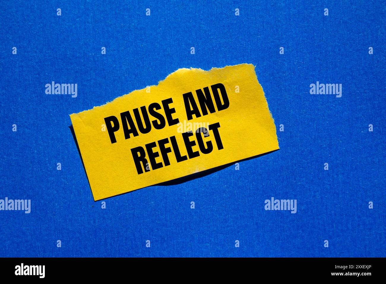 Pause and reflect message written on ripped torn yellow paper piece with blue background ...