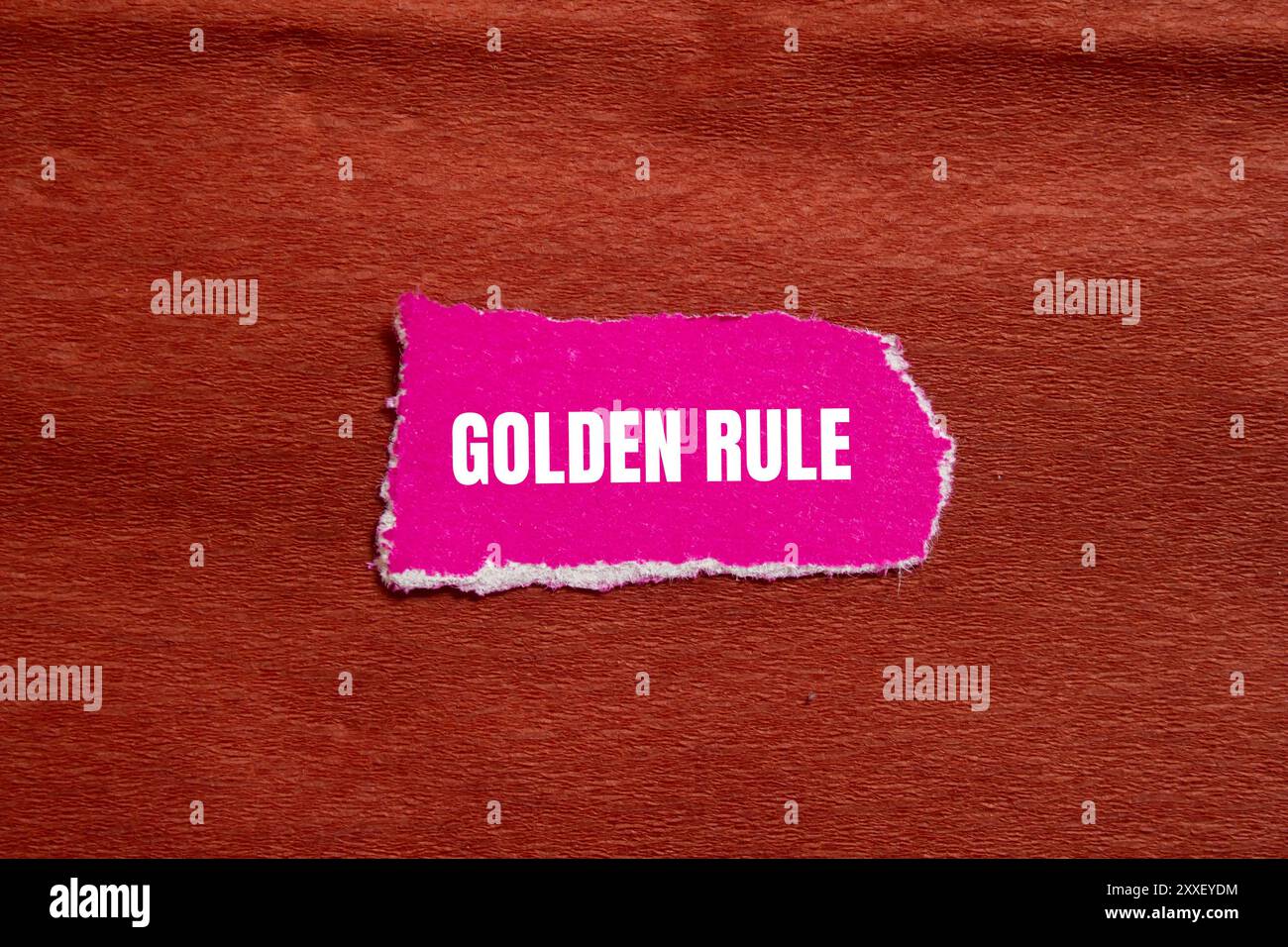 Golden rule message written on ripped torn pink paper piece with brown background. Conceptual ...