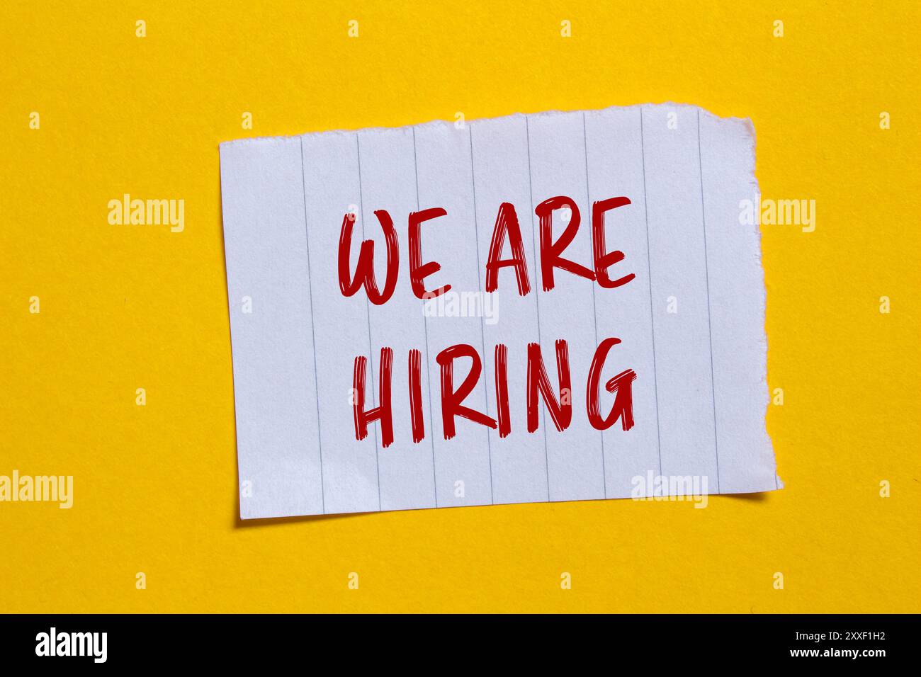 We are hiring message written on ripped torn white paper piece with yellow background ...