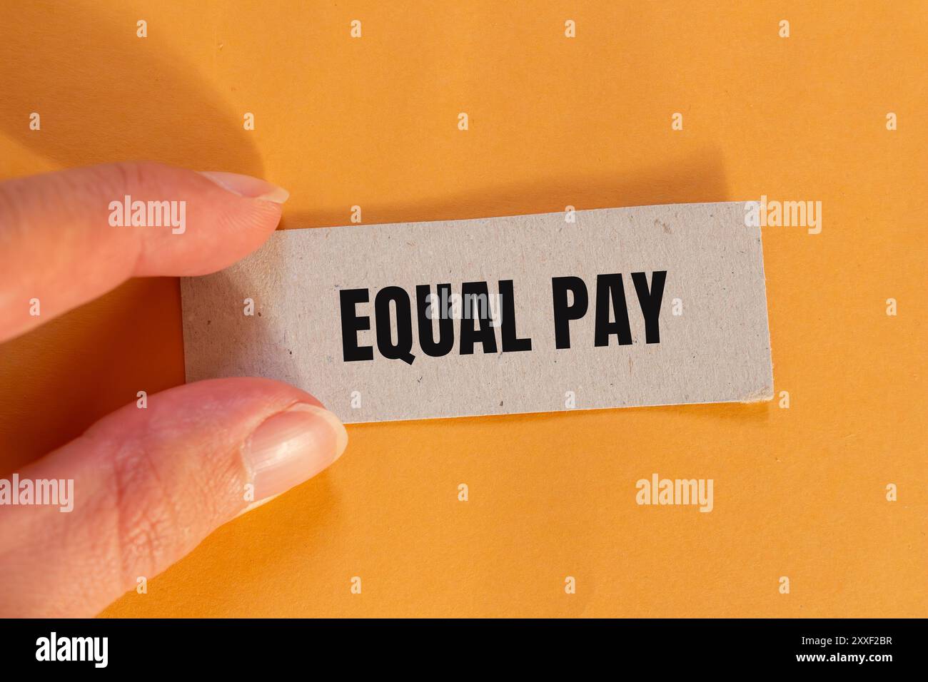 Equal pay message written on ripped paper piece with orange background ...