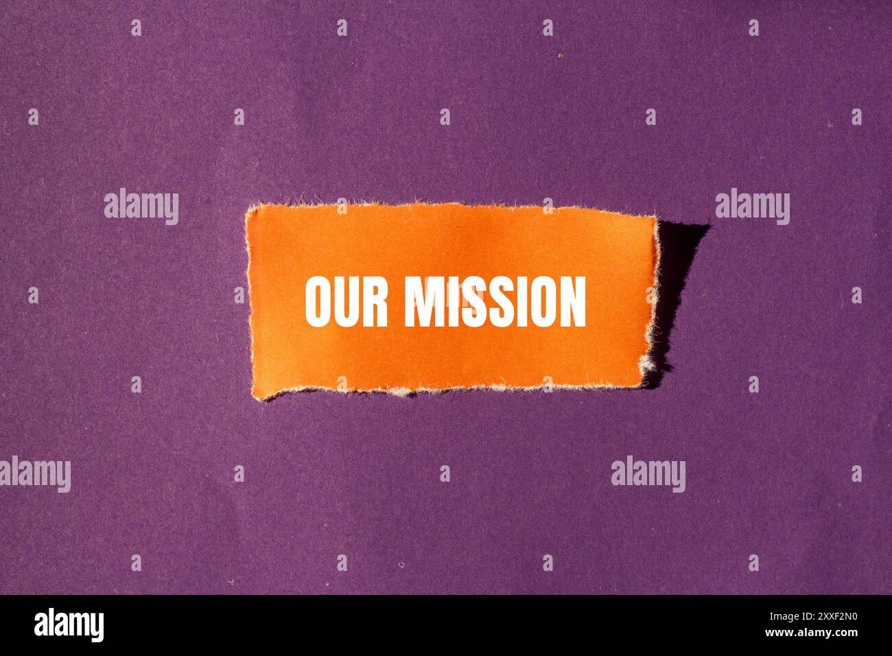 Our mission message written on ripped torn orange paper piece with purple background. Conceptual ...