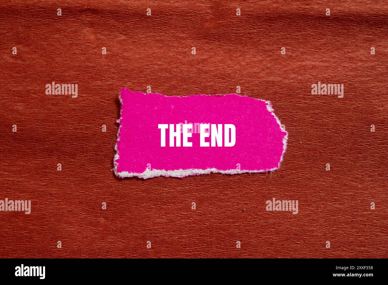 The end message written on ripped torn pink paper piece with brown background. Conceptual the ...