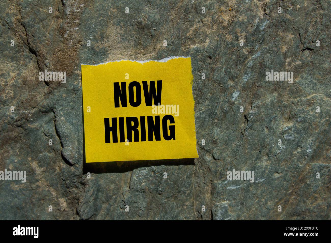 Now hiring message written on ripped yellow torn paper piece with stone background. Conceptual ...
