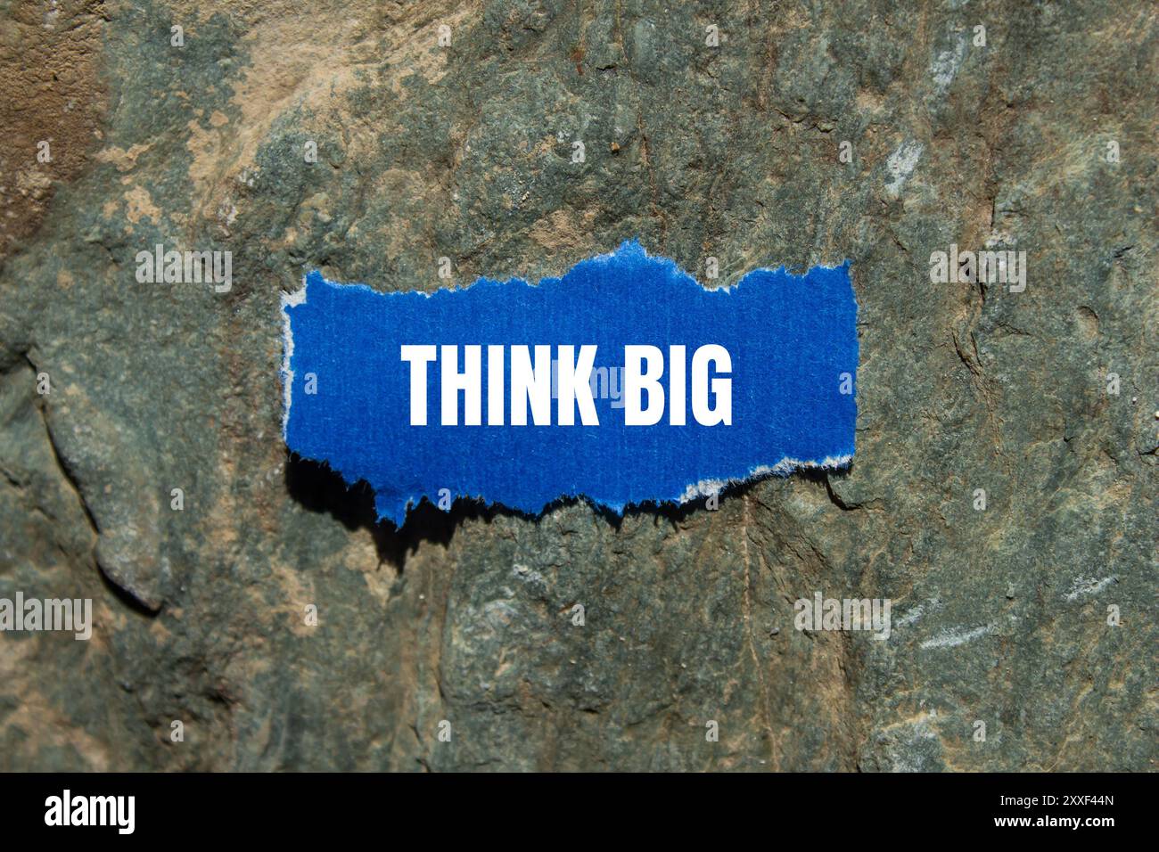 Think big message written on ripped torn blue paper piece with stone ...