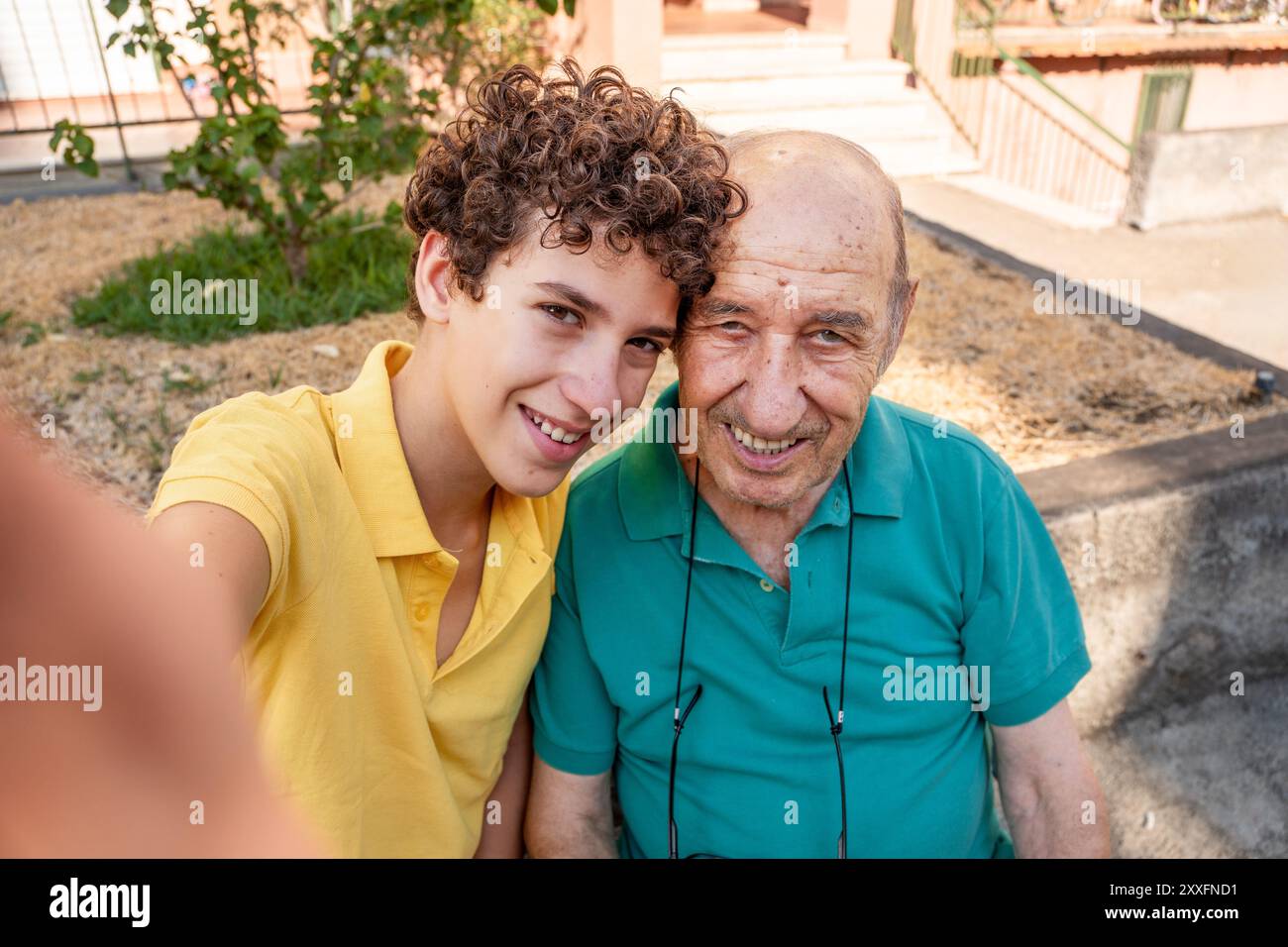 Joyful curly-haired teenager taking selfie with smiling elderly ...