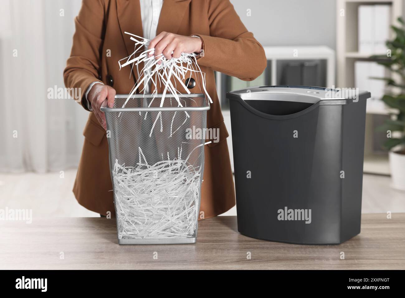 Woman putting shredded paper strips into trash bin at wooden table in ...