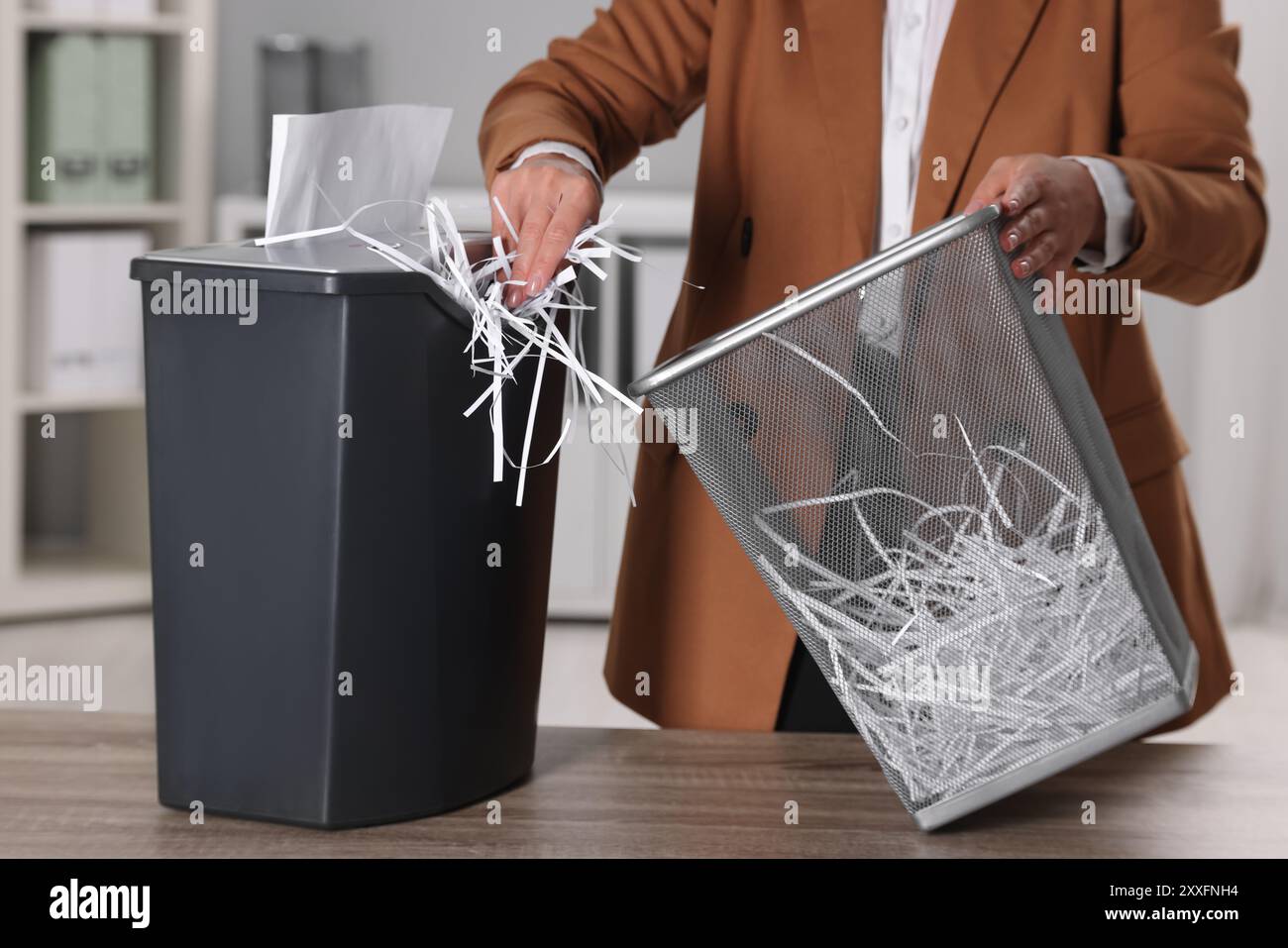 Woman putting shredded paper strips into trash bin at wooden table in ...