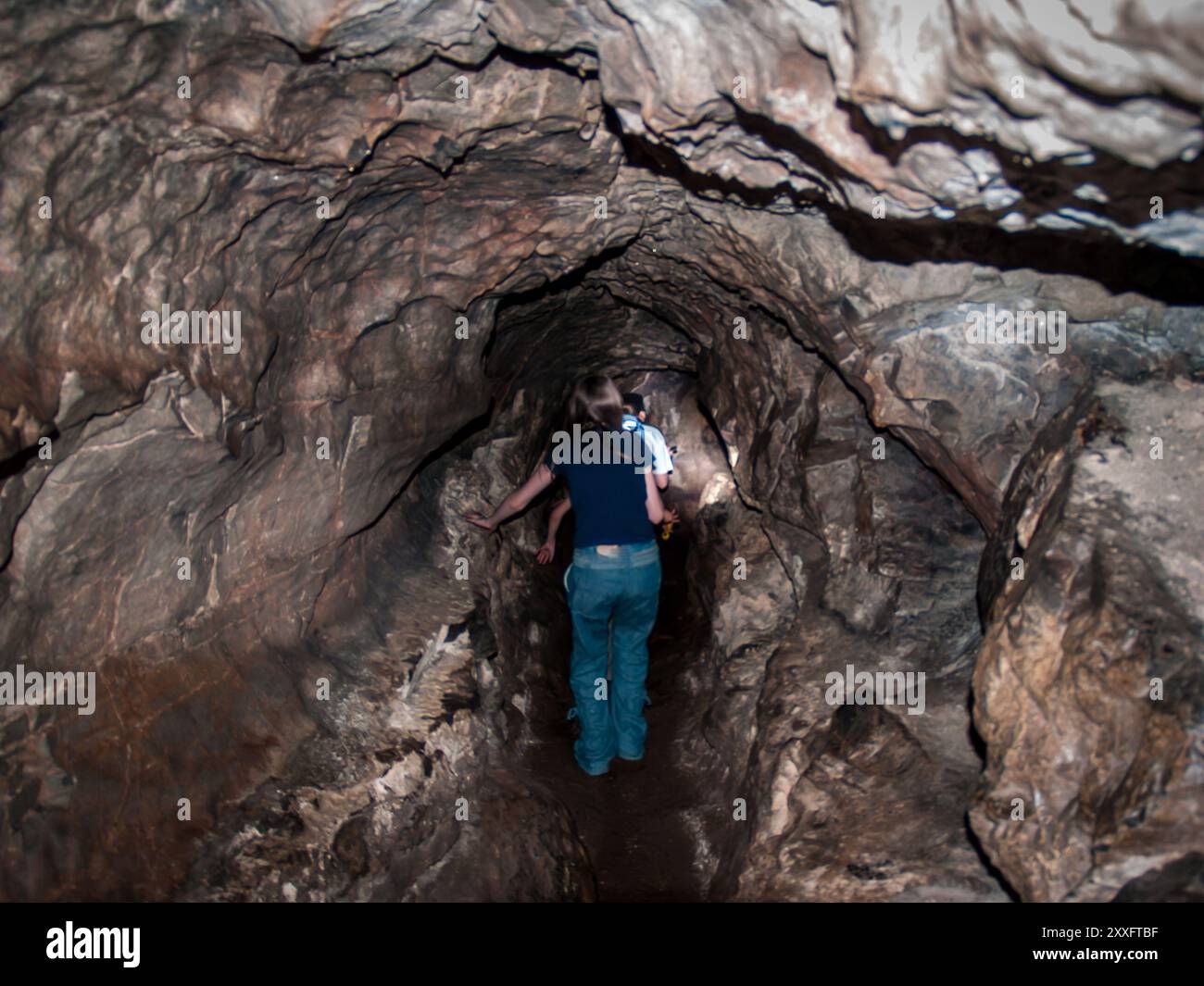 Visitors using torches to explore the limestone cave and dark tunnel ...