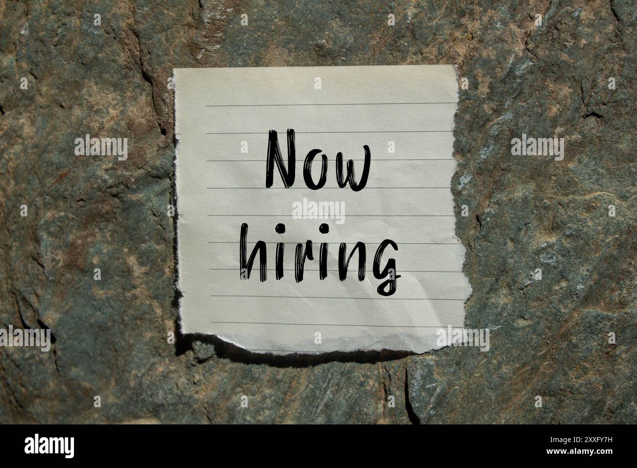 Now hiring message written on ripped torn paper piece with stone background. Conceptual now ...