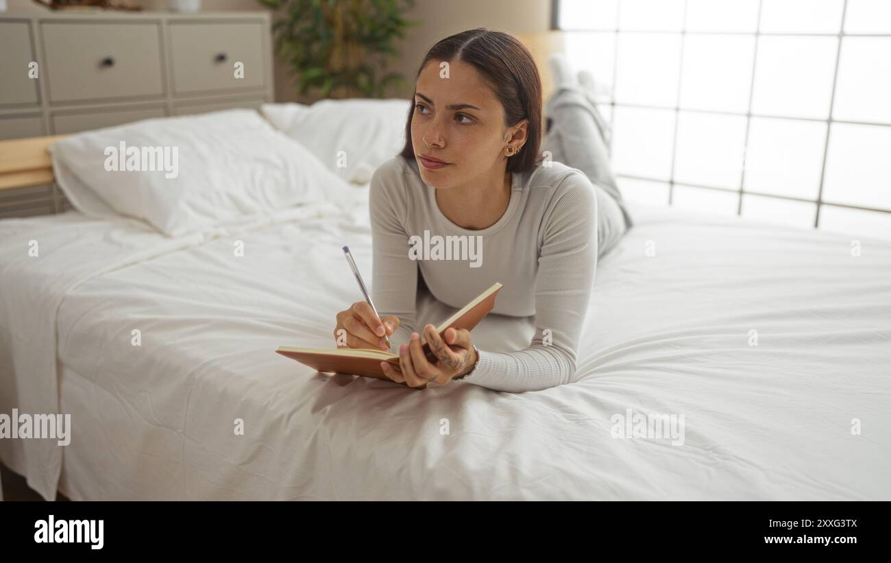 Young woman writing in a notebook while lying on a bed in a home ...