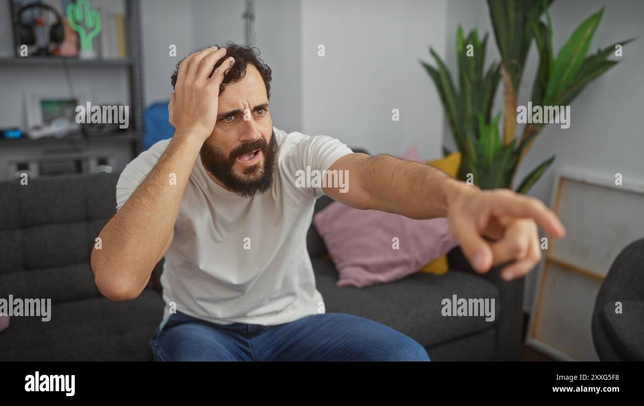 A confused man with a beard points and scratches his head in an indoor ...