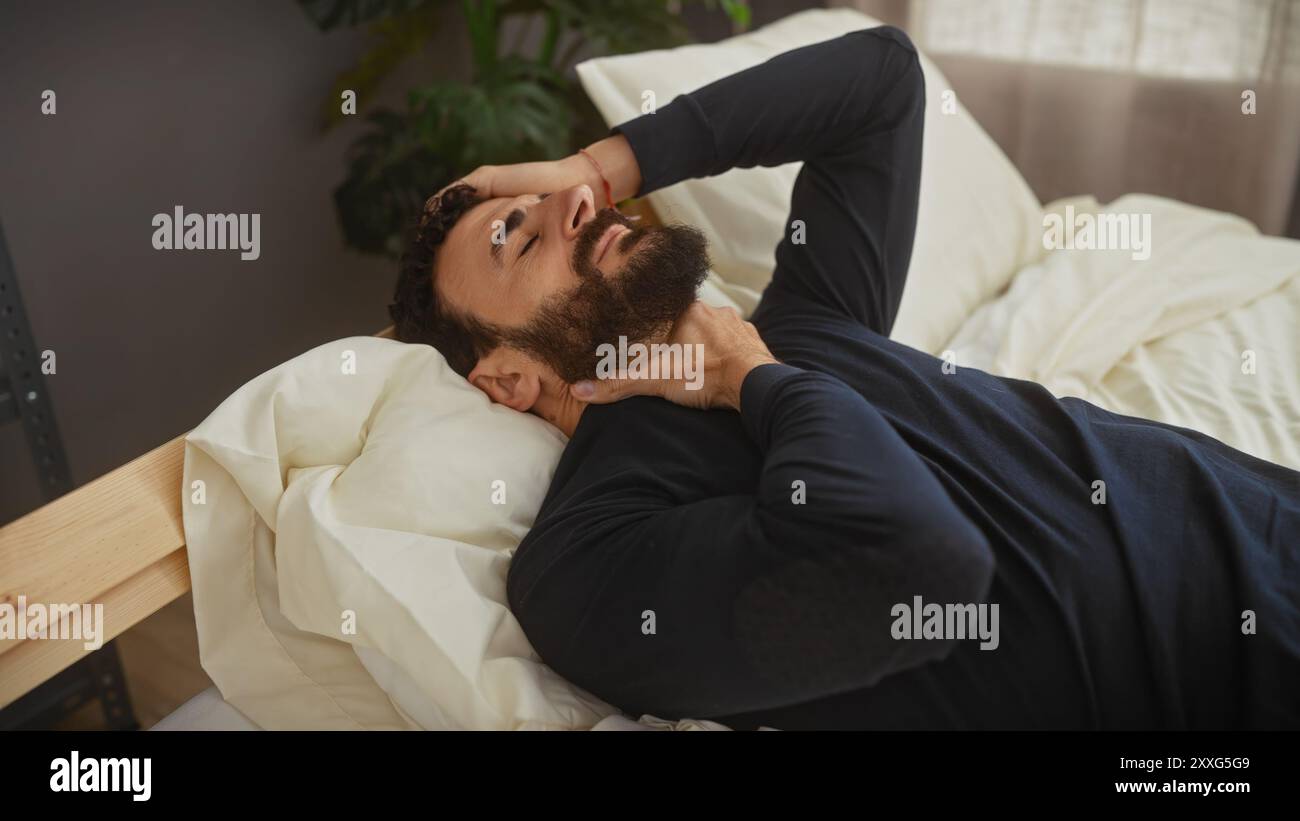A bearded middle-aged man in a bedroom appears in discomfort or pain ...