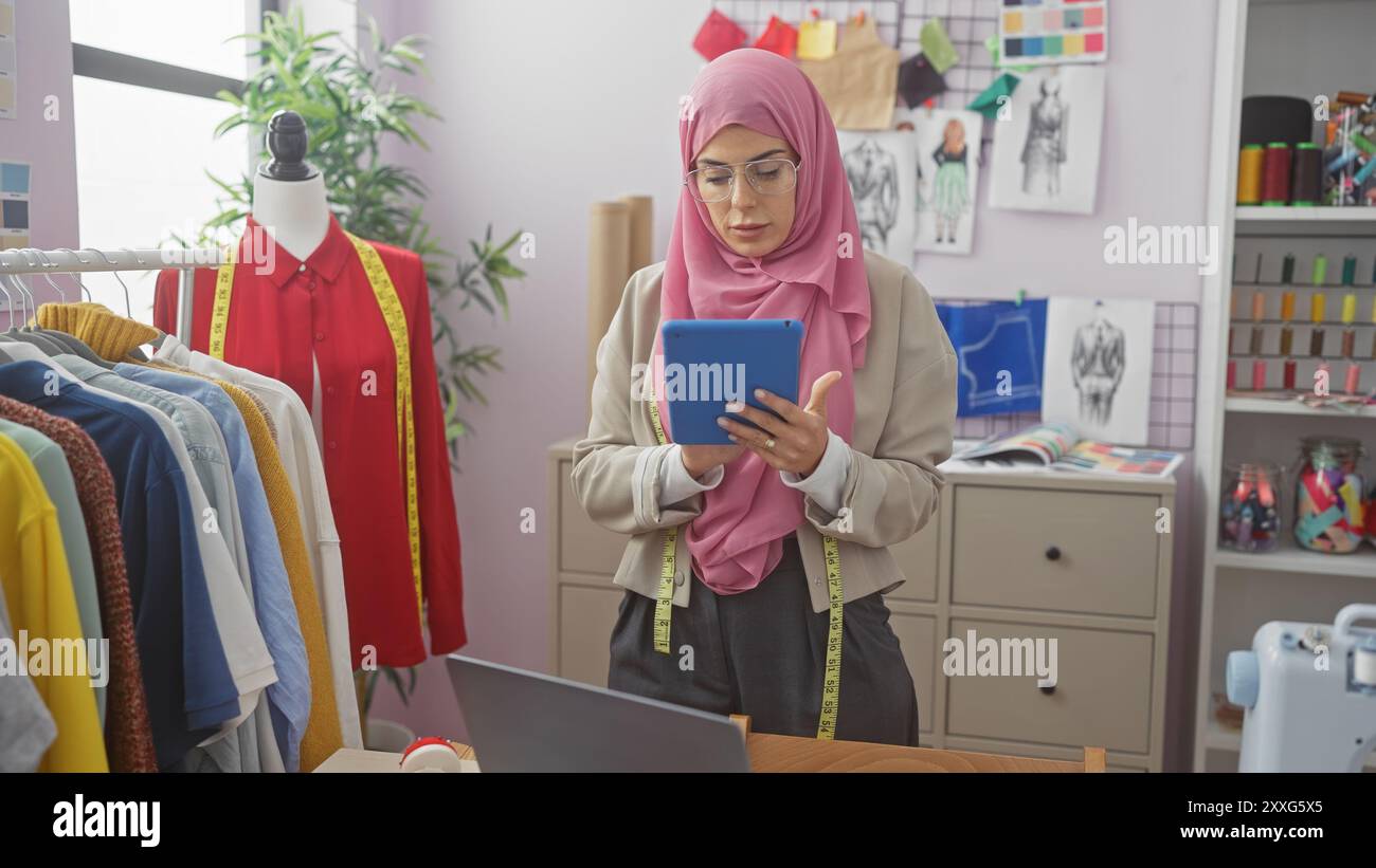 Muslim woman tailor with tablet standing in her modern atelier ...