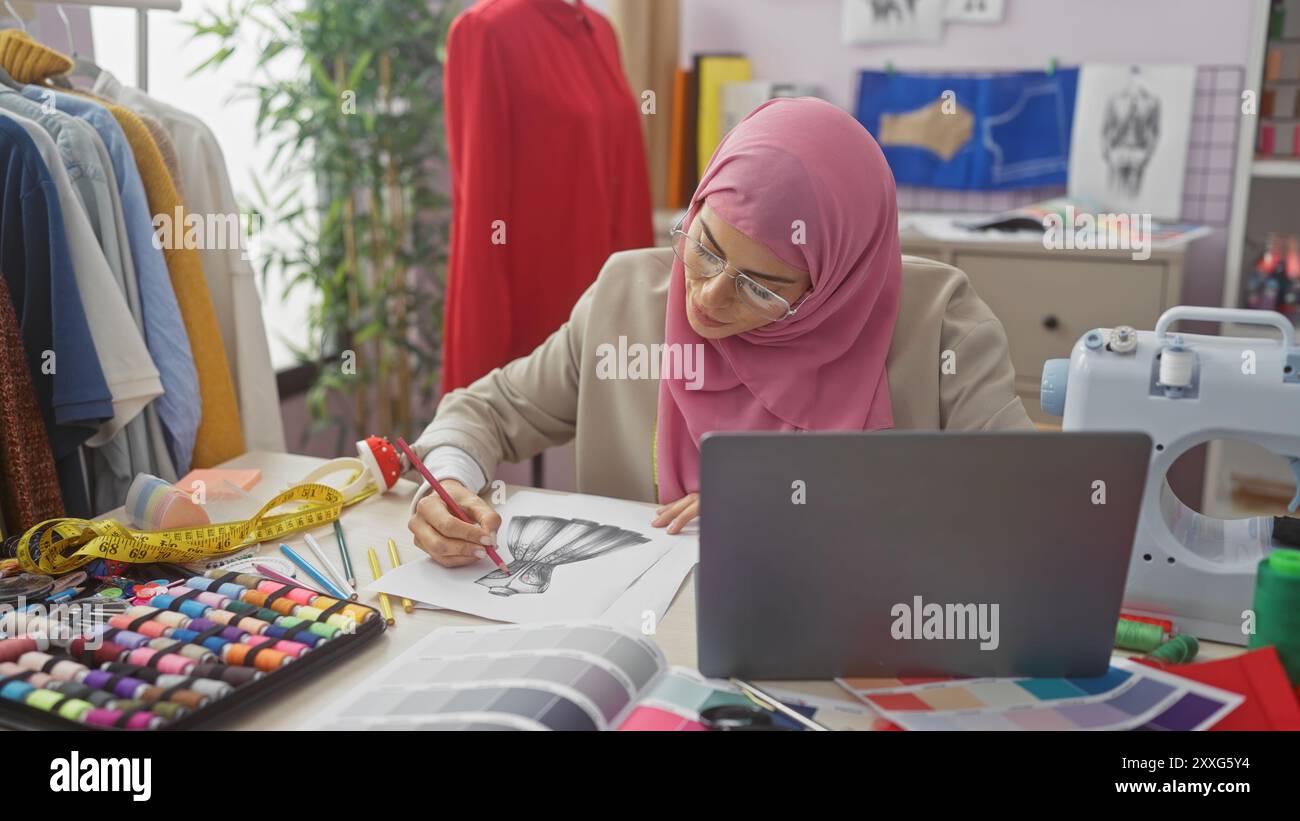 A focused woman in a hijab sketches a dress design in a bright ...