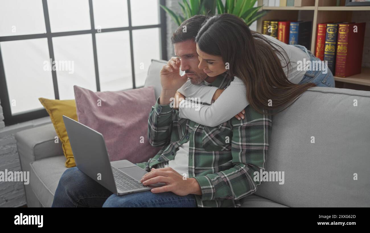 A worried couple, a man and woman, comfort each other on a sofa in a ...