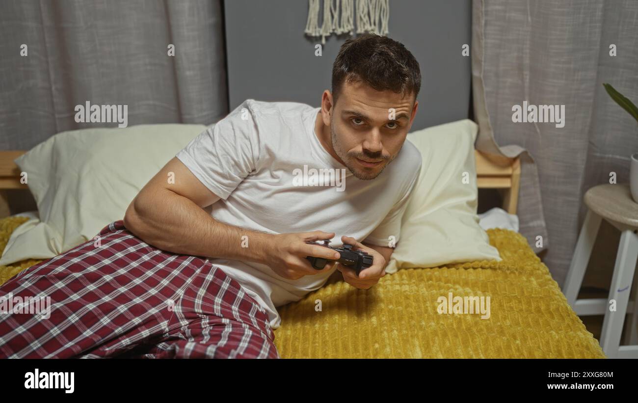 Hispanic man with a beard in his bedroom playing video games on the bed ...