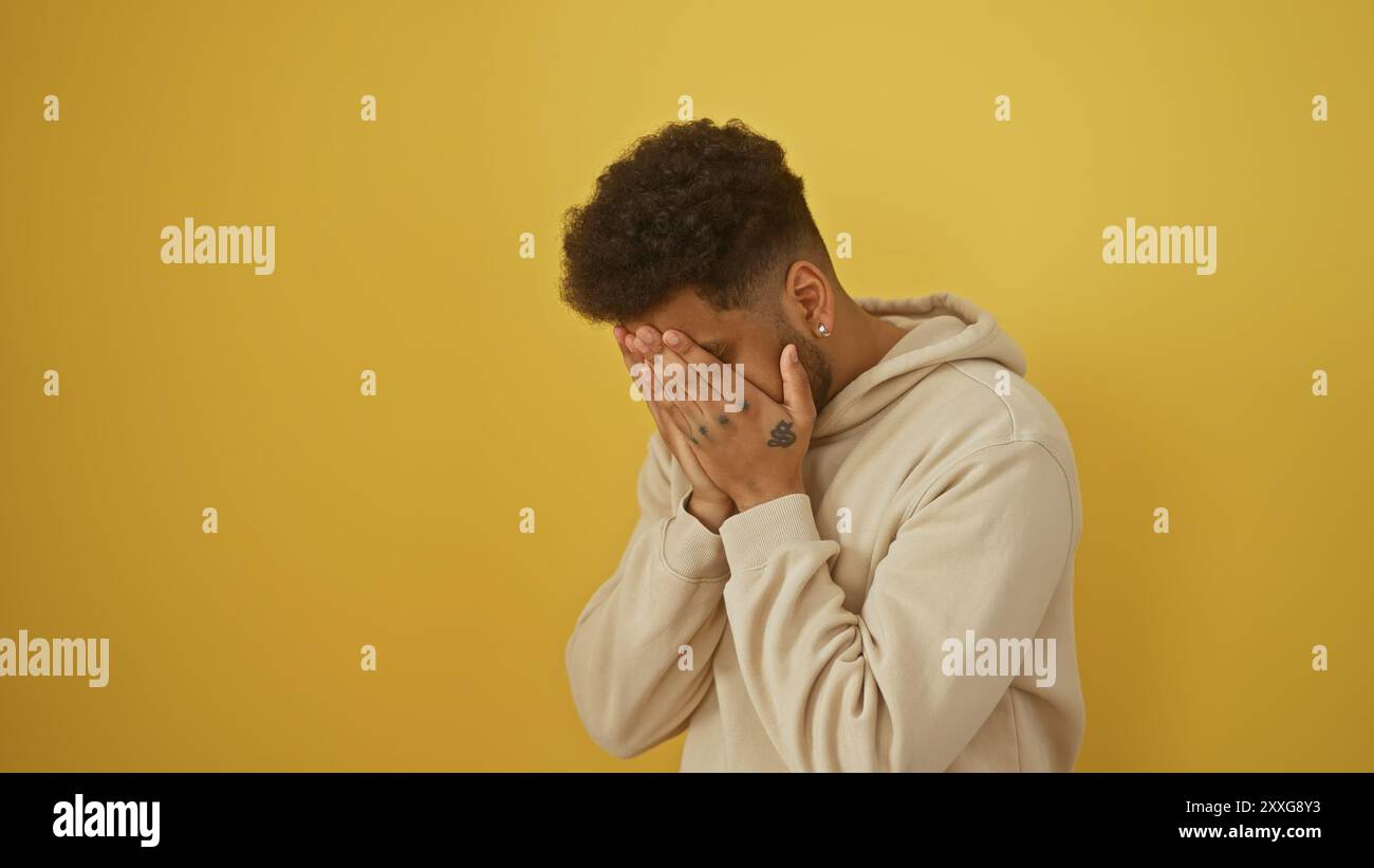 A distressed man covers his face with his hands against a yellow ...