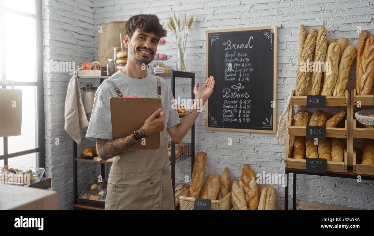 Young hispanic man with beard and clipboard in bakery shop pointing at ...