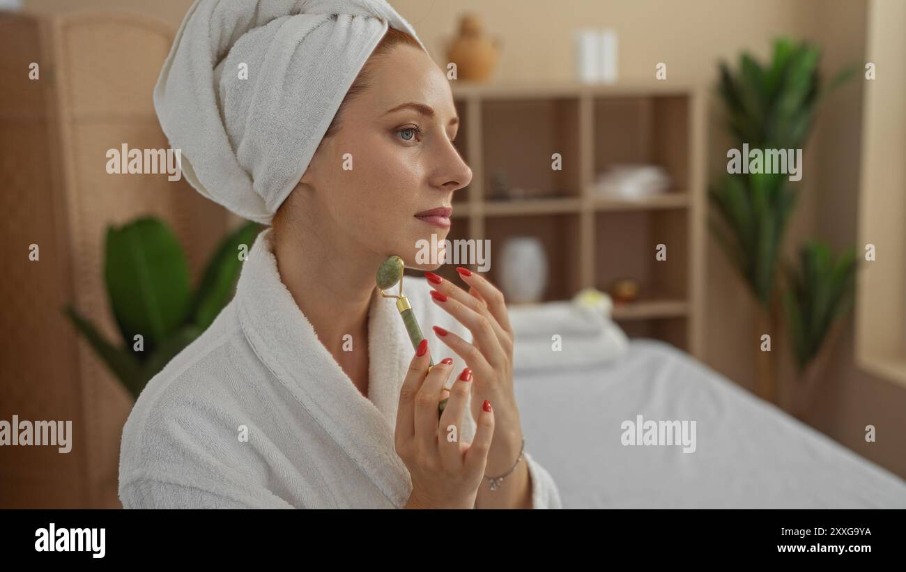 Woman applying jade roller in spa room looking relaxed wearing robe ...