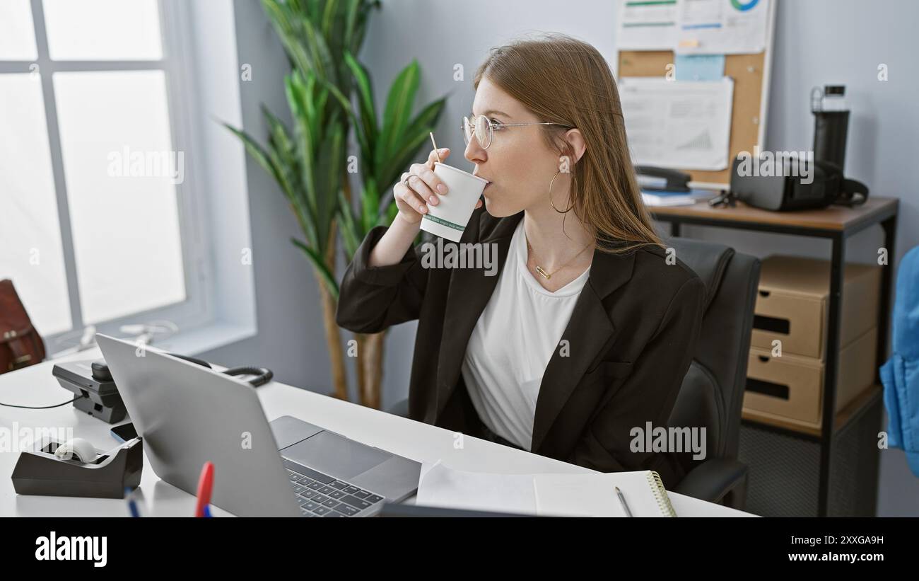 A young professional woman enjoys a coffee break at her modern office, reflecting a typical ...