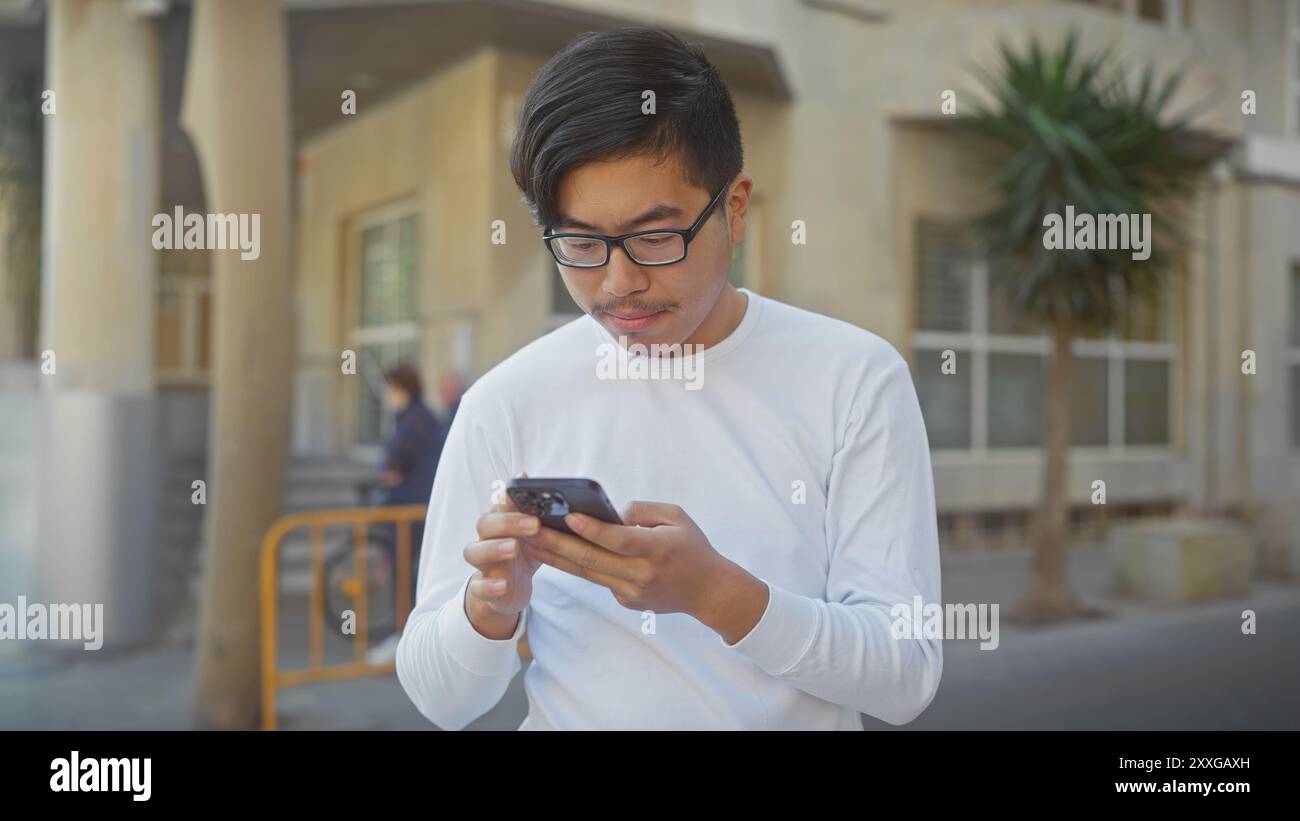 Young asian man using smartphone on a bustling city street, embodying ...